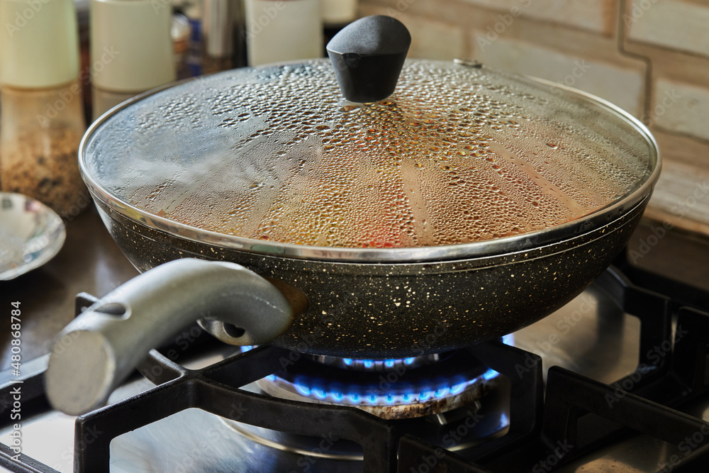 Frying pan on gas stove with the texture of drops on a glass lid with ...