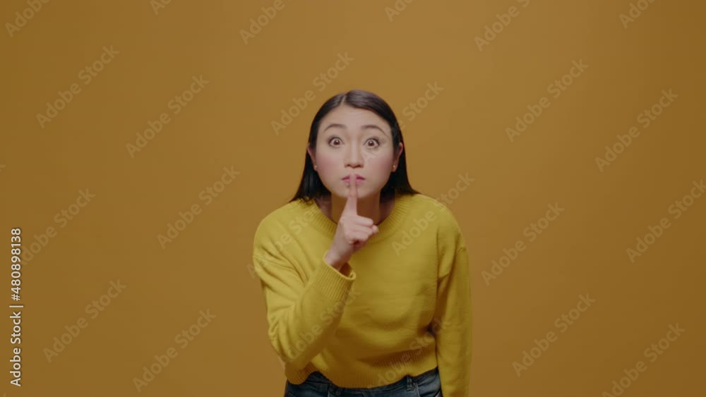 Asian woman doing silent gesture with index finger over lips in studio ...