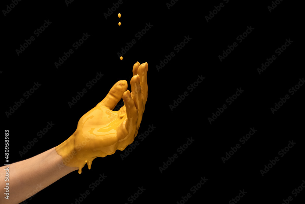 Yellow painted human hand gesturing isolated on dark studio background ...