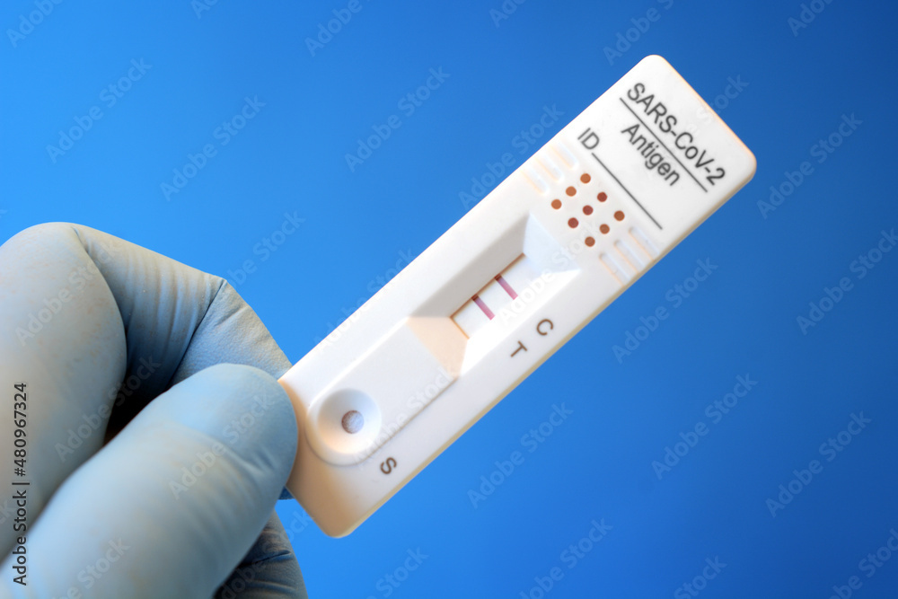 Doctor in a testing centre shows a rapid antigen test with a positive ...