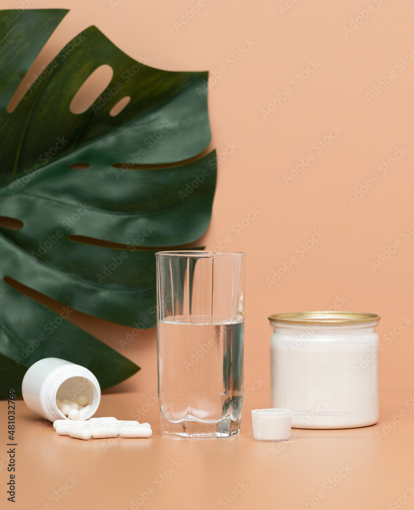 Collagen powder in a jar, tablets and water on a beige background with ...