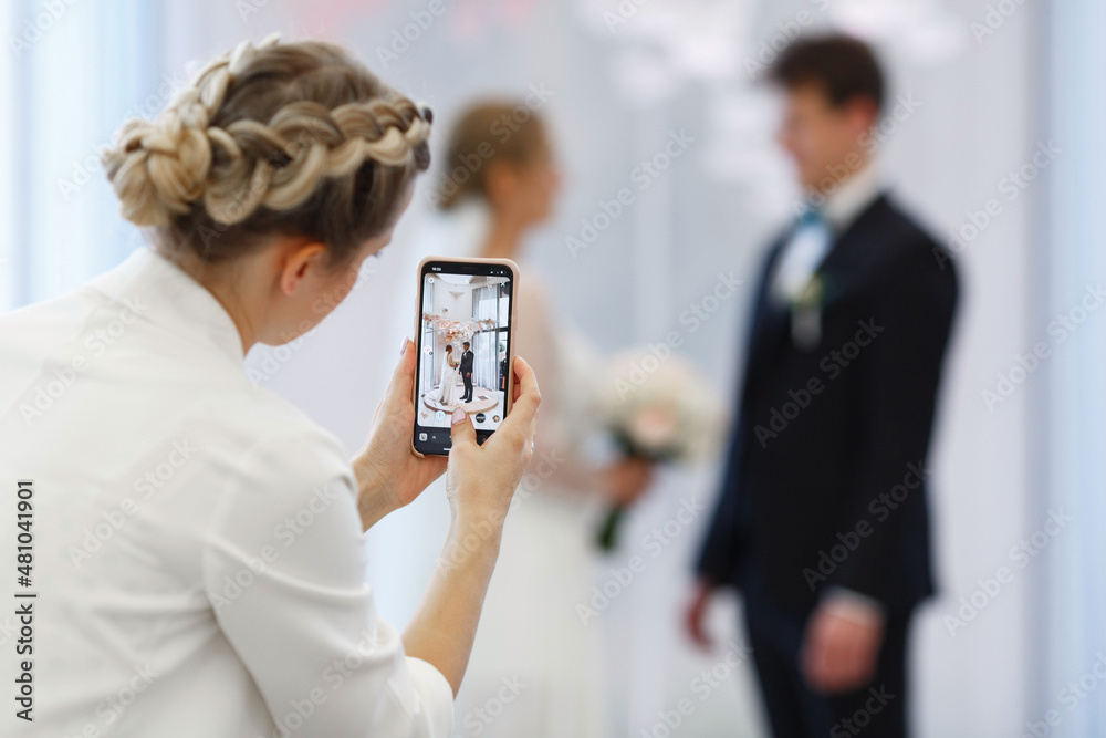 stylish woman with phone in hand take photo of wedding ceremony. guest ...