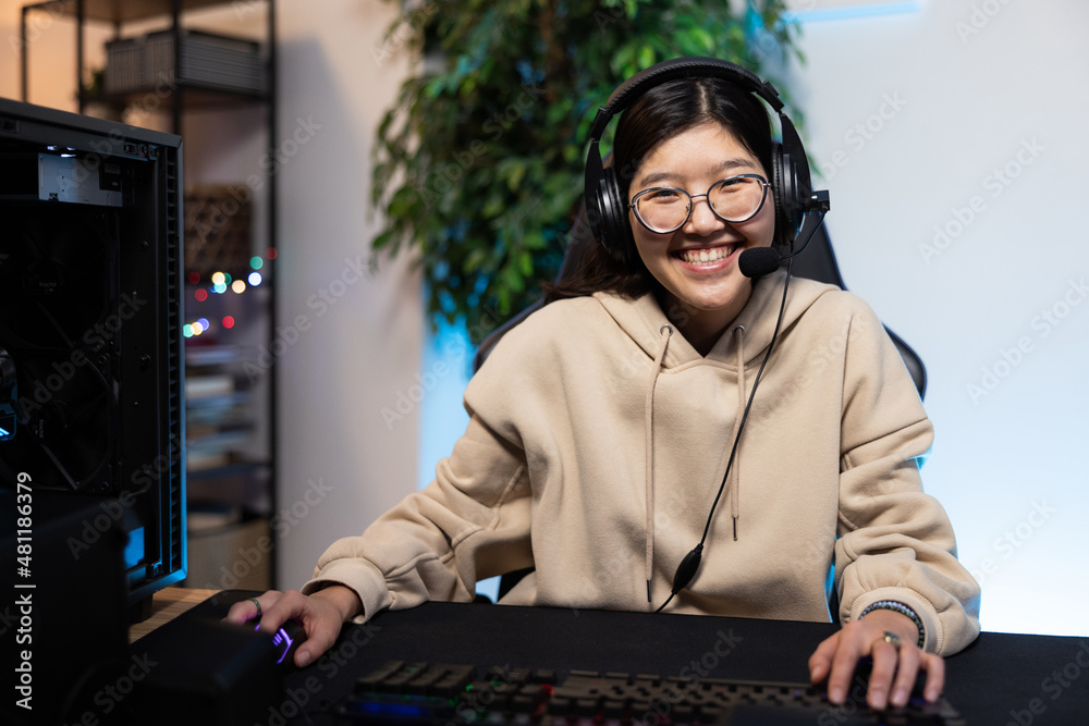 Joyful laughing professional Asian girl gamer wearing headphones with ...