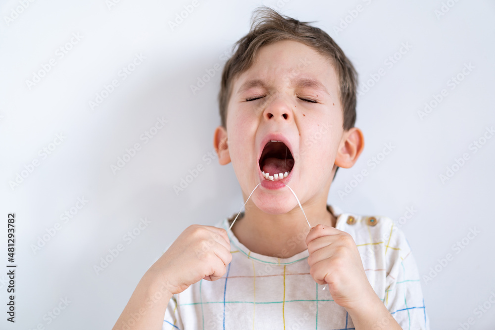 Cute boy pulling loose tooth using a dental floss. The boy's first milk ...