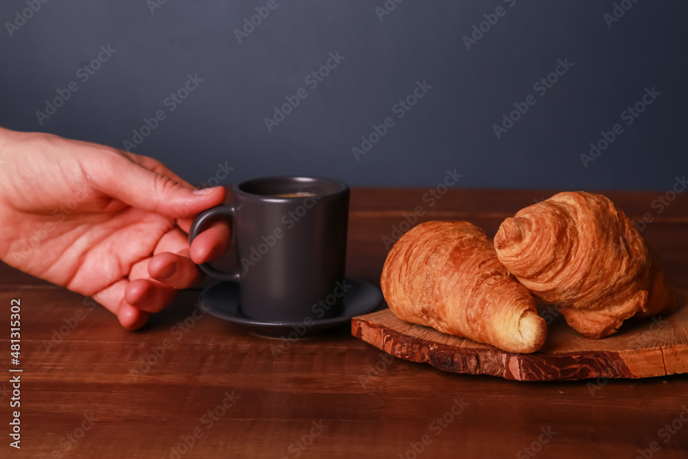 Human female hand holding black cup of espresso coffee, two croissants ...