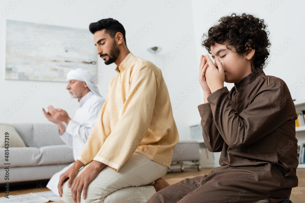 Muslim boy holding hands near face while praying near multiethnic ...
