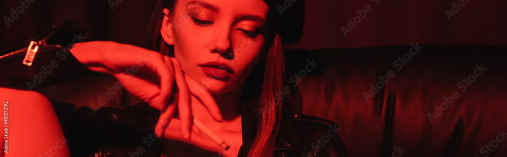 young sensual woman smoking in red light on black background, banner ...