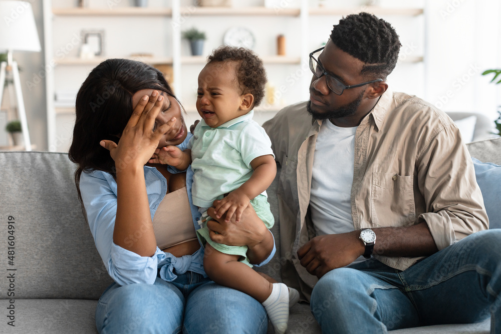 Tired African American parents sitting with crying kid on sofa Stock ...