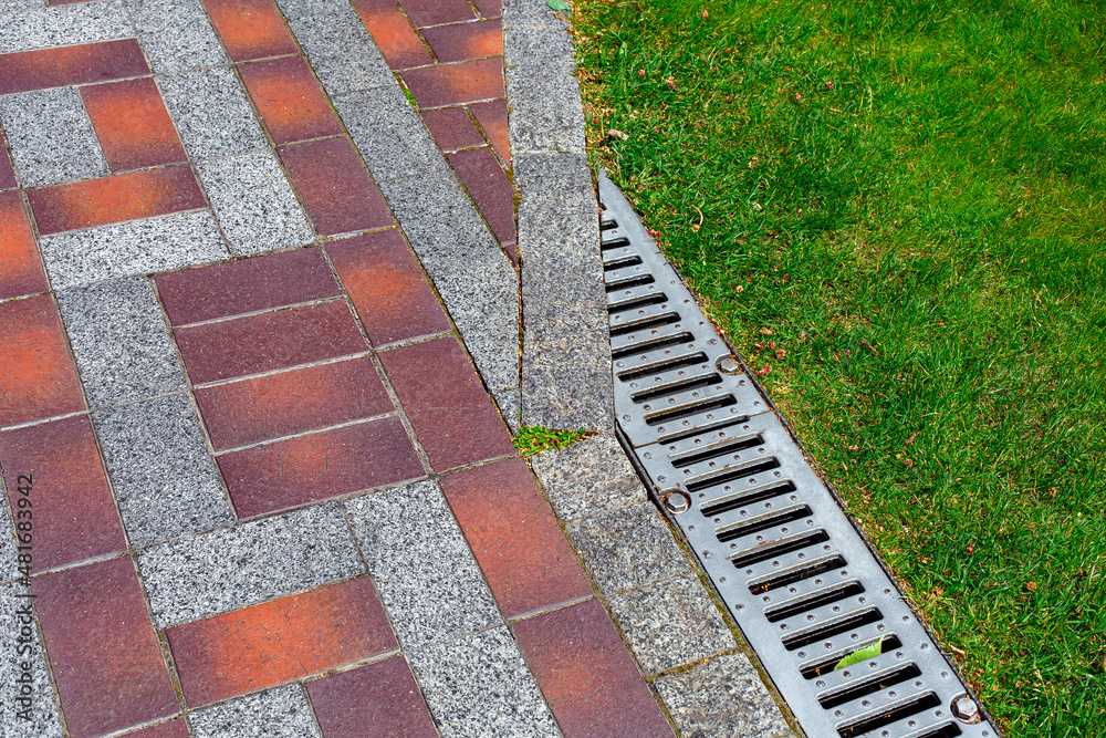 drainage grate bolted to storm drain at corner of pedestrian pavement ...