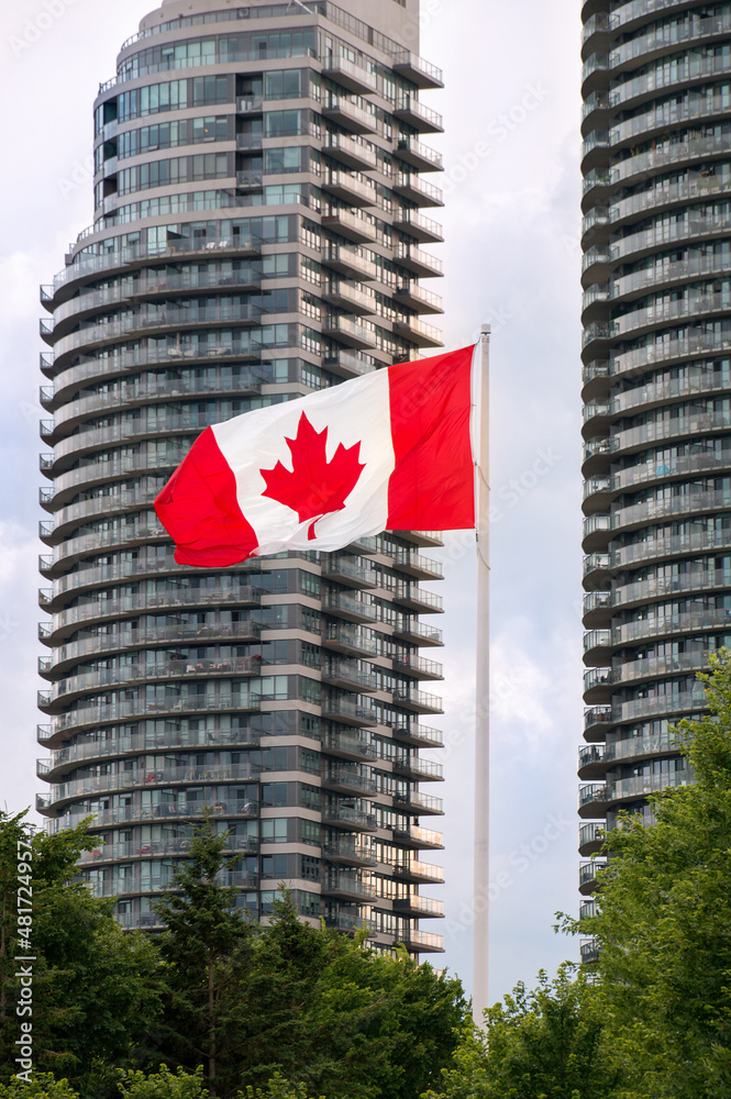 Red and white Canadian flag waving on the mast above the park trees in ...