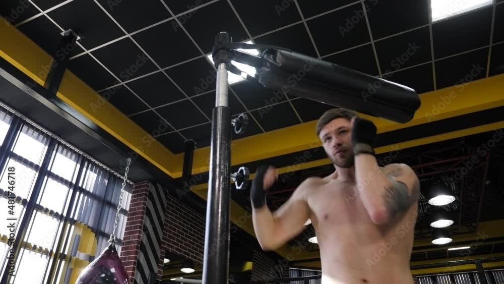 A strong male boxer trains on a rotating boxing simulator, punches a ...