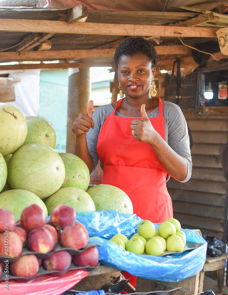 African woman or female trader with a red apron, standing at her stall ...