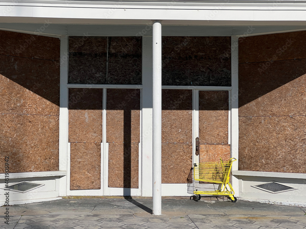 A boarded up storefront with an abandoned yellow shopping cart. Concept ...