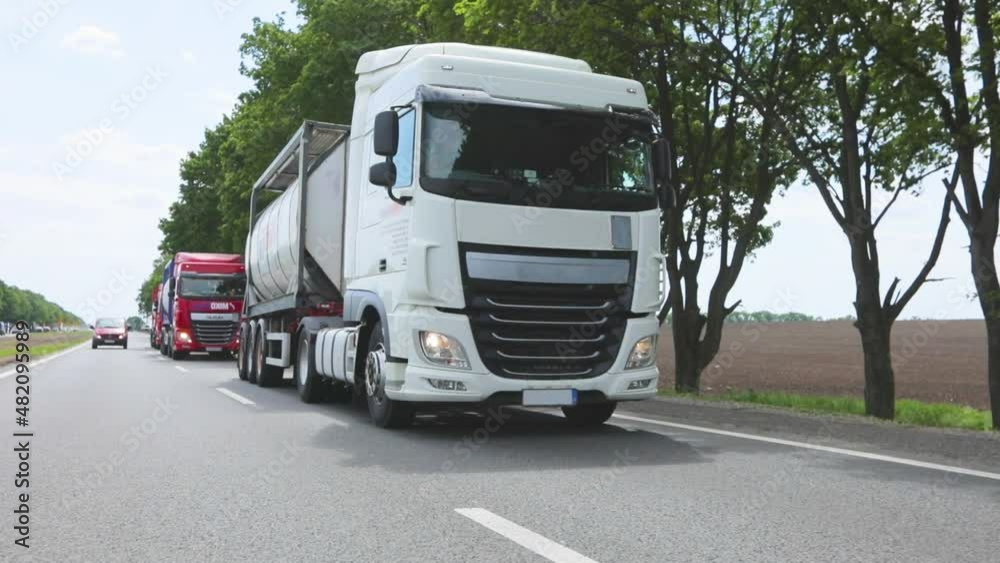 Trucks are driving along the road. A truck with a tank truck drives ...