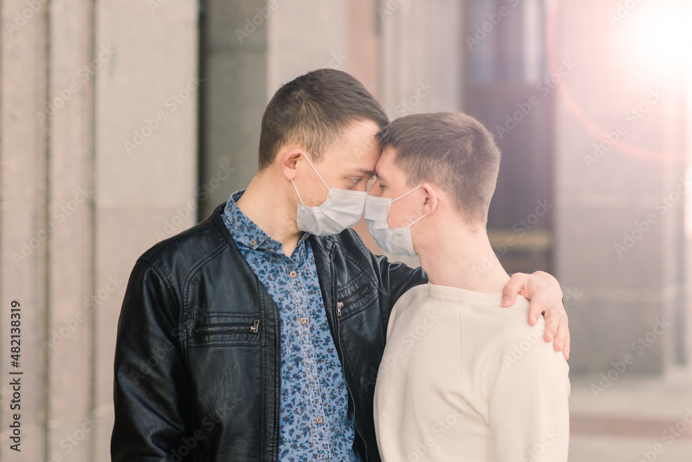 Young gay couple wearing medical mask, hugging and kissing at the city. Stock Photo | Adobe Stock