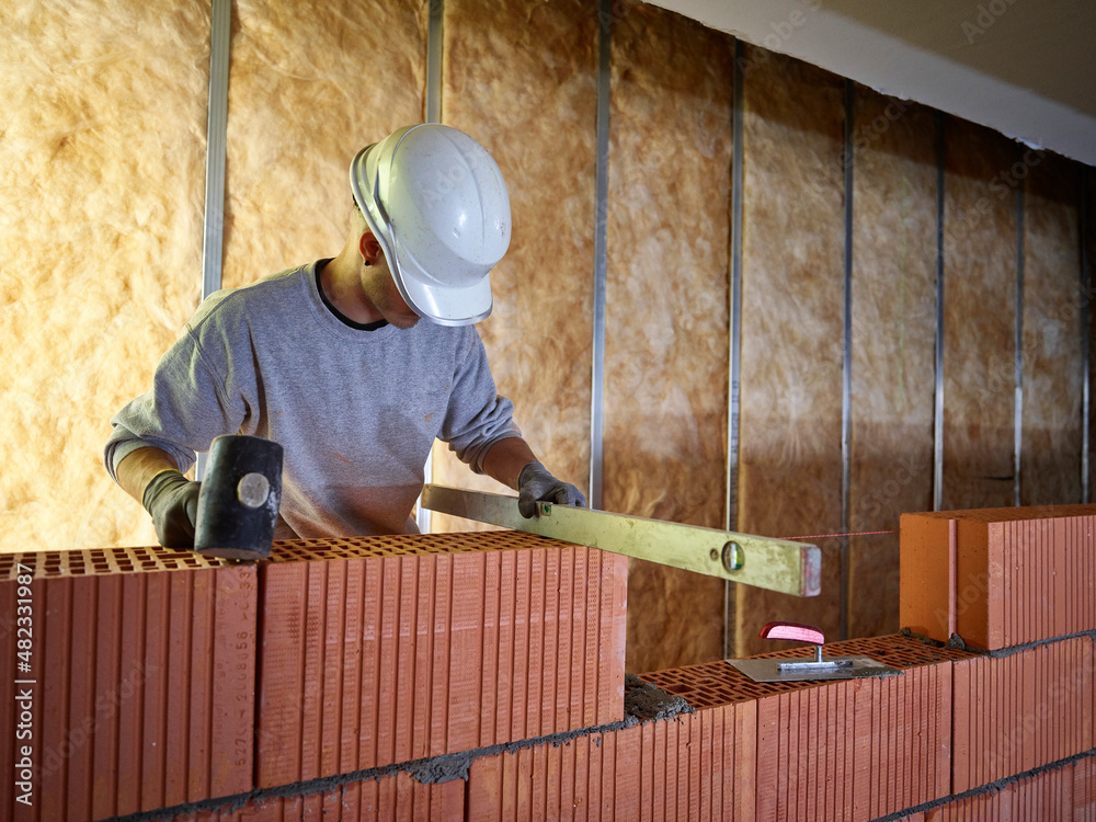 Bricklayer with hammer using spirit level on bricks at construction ...