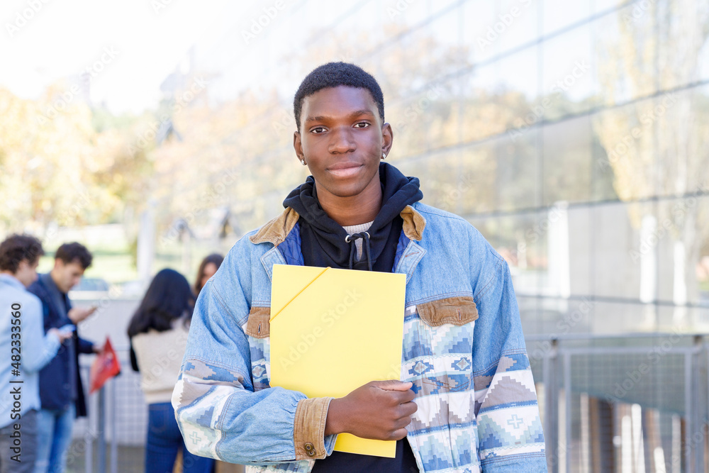 Teenage student holding yellow file at campus Stock Photo | Adobe Stock