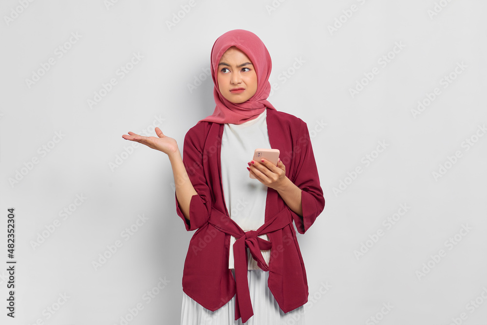 Confused beautiful Asian woman in casual shirt and hijab using mobile ...