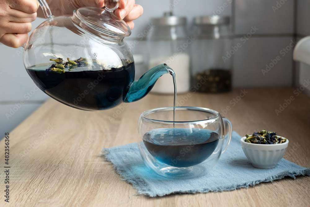 Hands pouring anchan from teapot into cup, butterfly pea flower tea ...