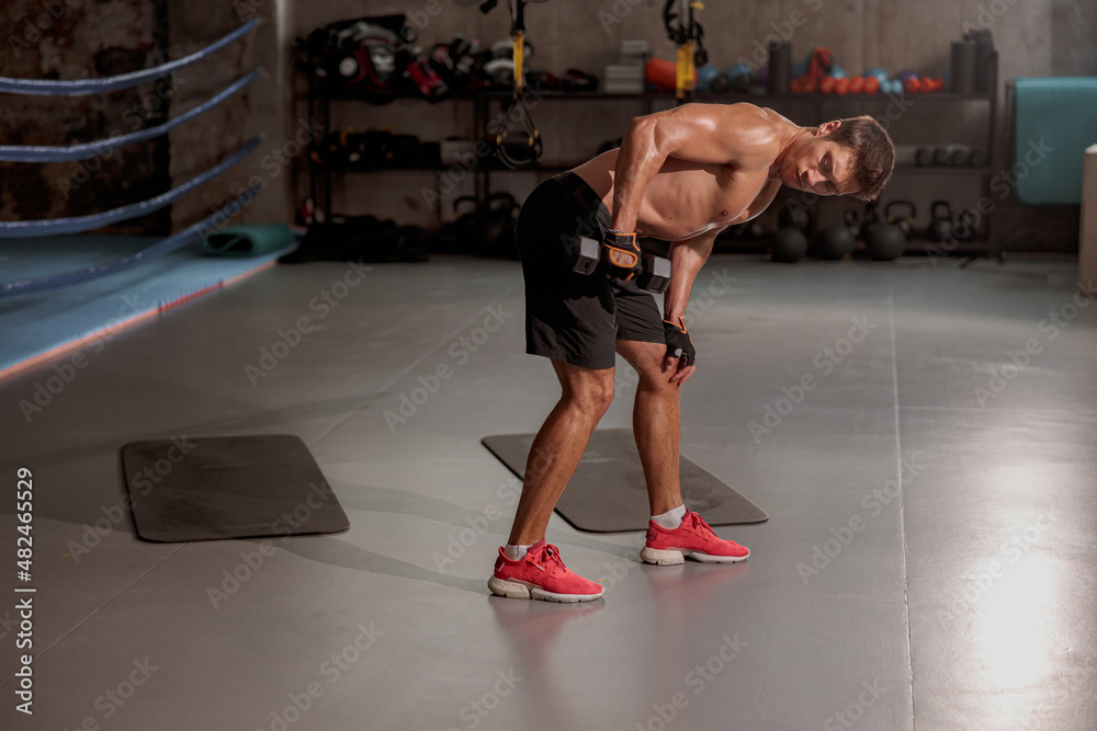 Strong man standing leaning forward and holding black dumbbell while ...