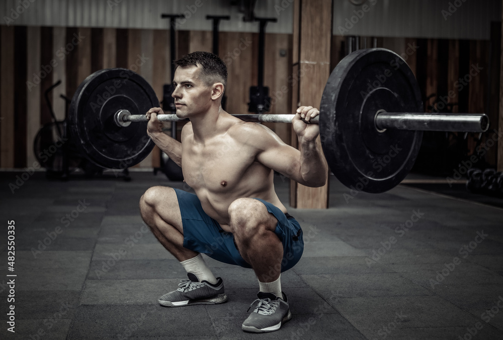 Young muscular male bodybuilder doing squats with a barbell on his ...