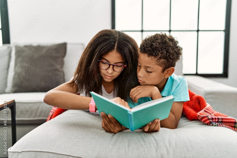 Two siblings lying on the sofa reading a book checking the time on ...