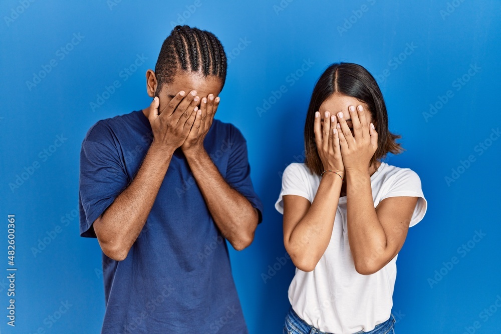 Young hispanic couple standing together with sad expression covering ...