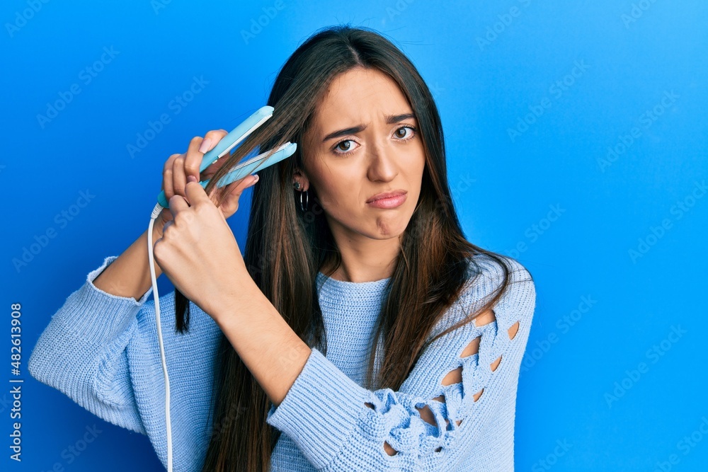 Young hispanic girl holding hair straightener depressed and worry for ...