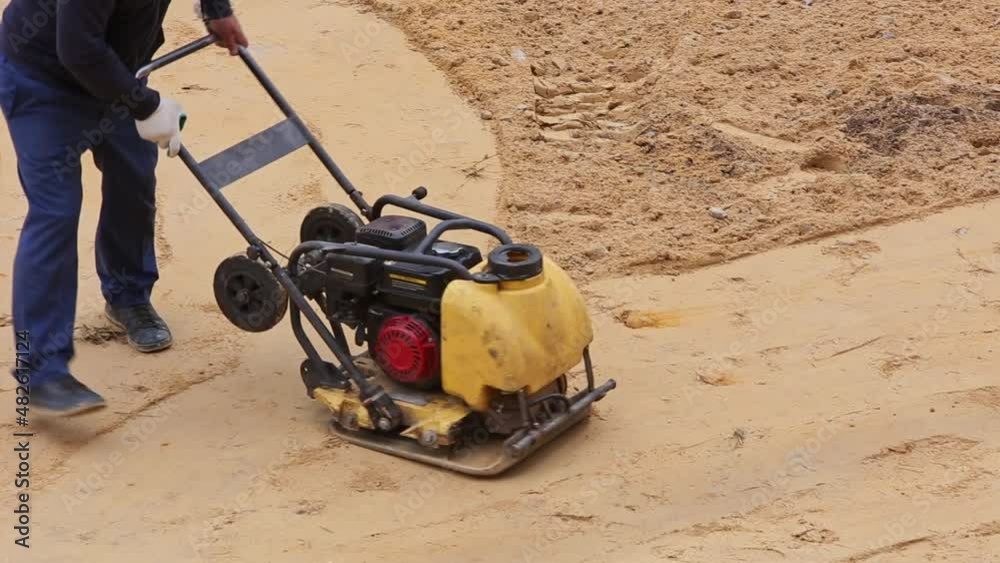 worker with vibration plate compactor ramming sand on construction site ...