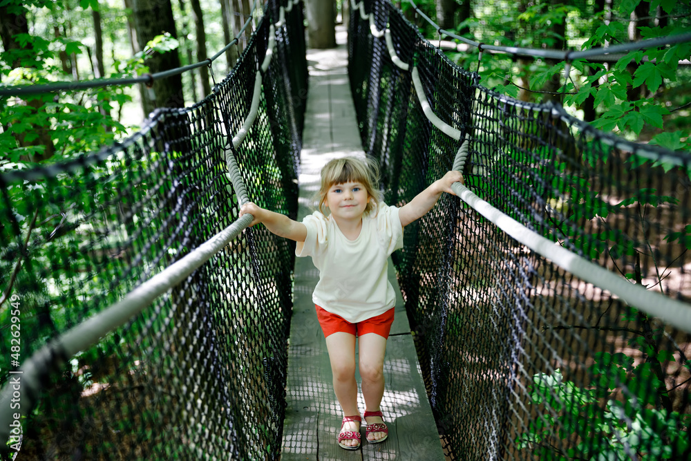 Cute little preschool girl walking on high tree-canopy trail with ...