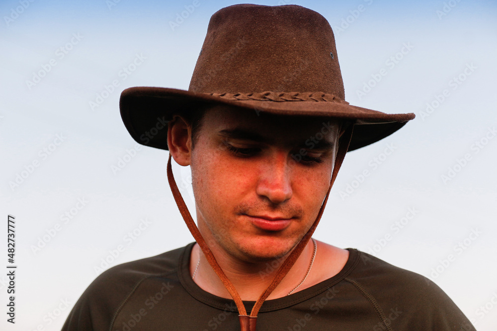 Young man smiling farmer in cowboy hat at field against blue sky ...