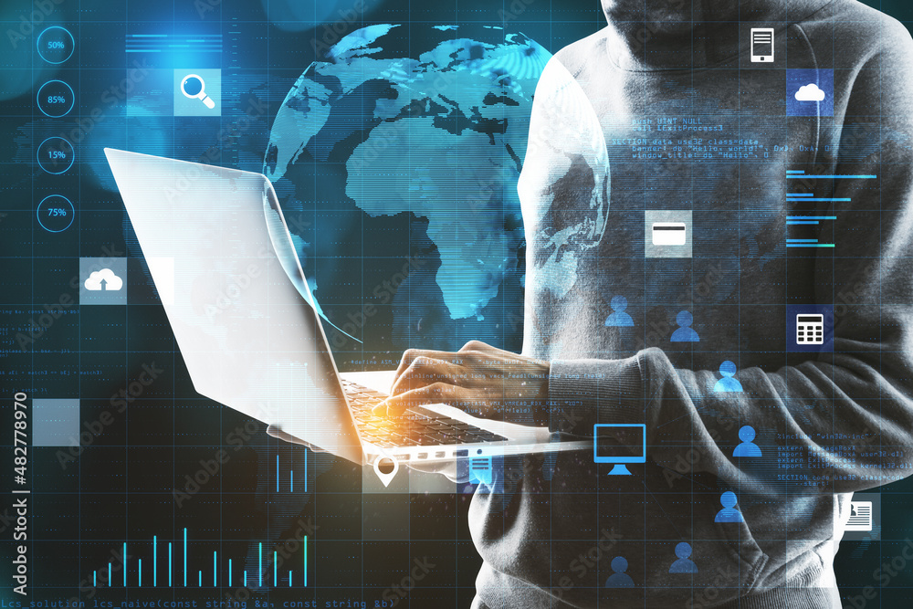 Hacker in hoodie using laptop with creative glowing globe hologram grid interface on blurry ...