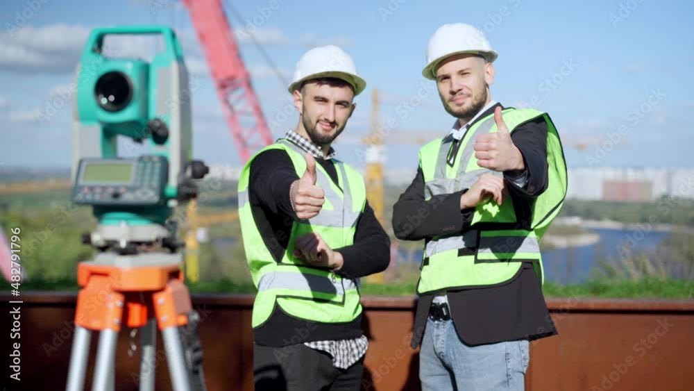 Two positive men gesturing thumbs up smiling looking at camera standing ...