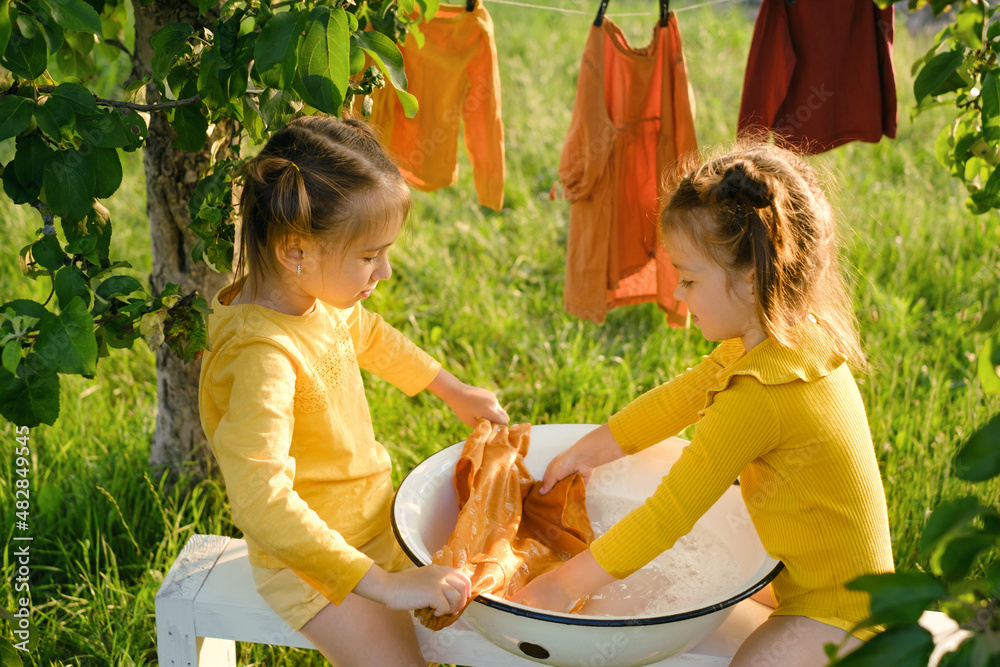 Kids wash clothes in a basin on a bench in the garden. Girls have fun ...