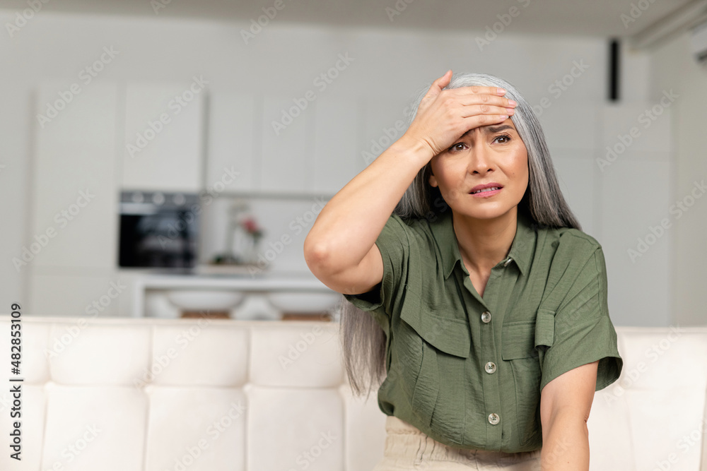 Worried gray-haired woman holding forehead with hand sitting on the ...