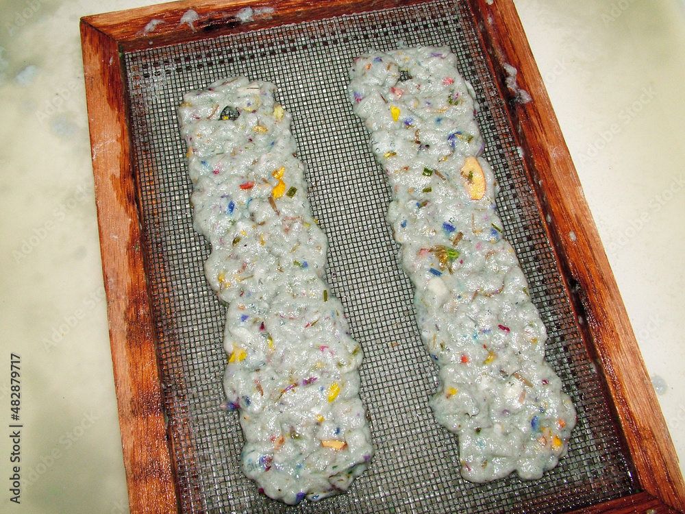 White paper pulp with flower petals in strips on a screen in a mold for ...