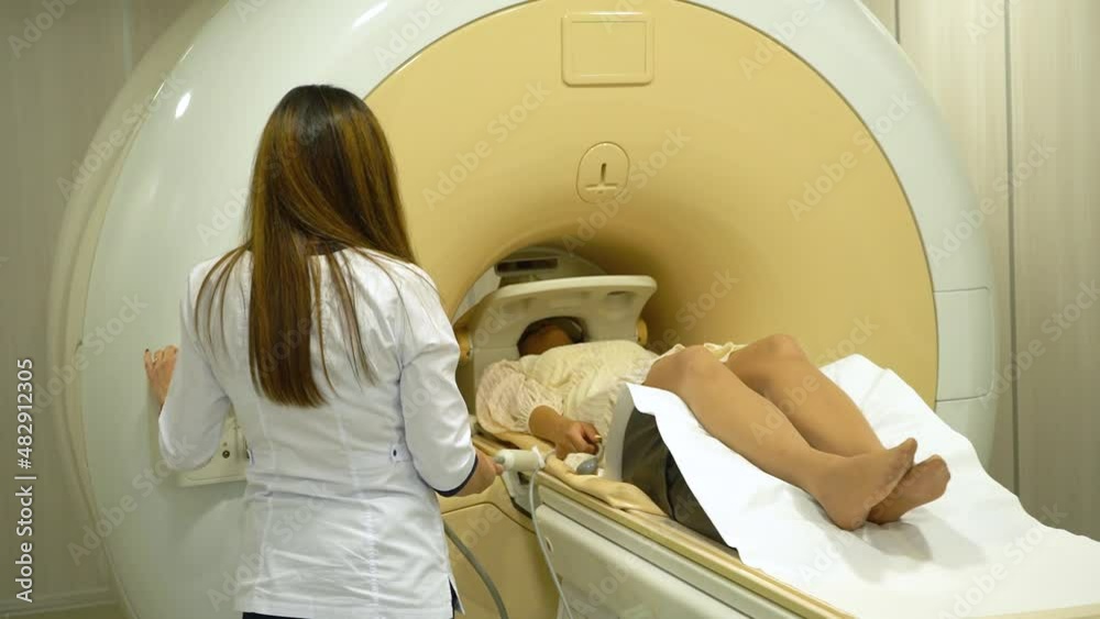 In a medical laboratory, a radiologist monitors an MRI with a patient ...
