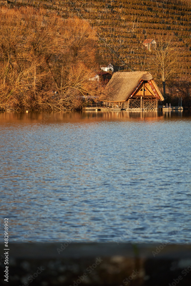 House on the lake in autumn. Brown building with thatched roof in front ...