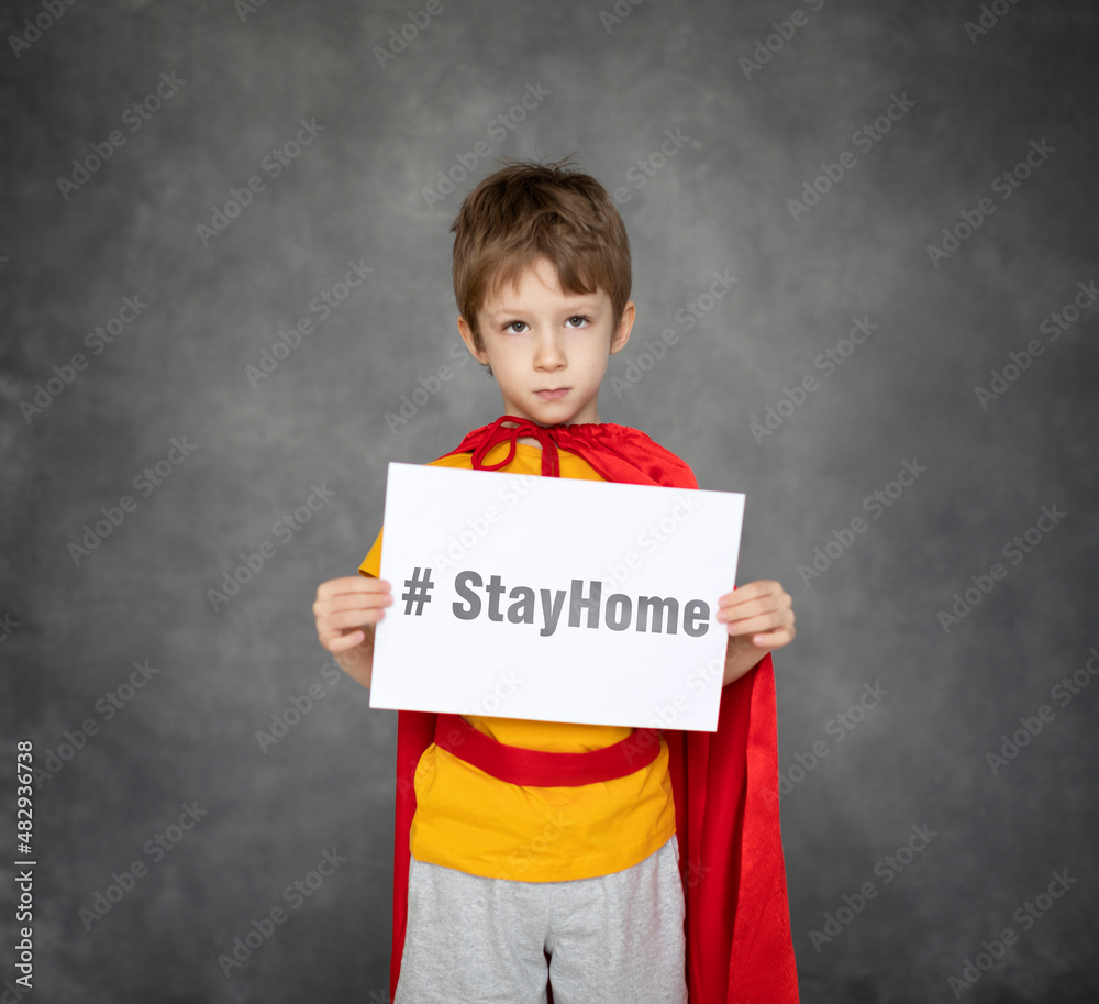 STAY HOME. Little serious sad boy in a superhero costume with a red ...