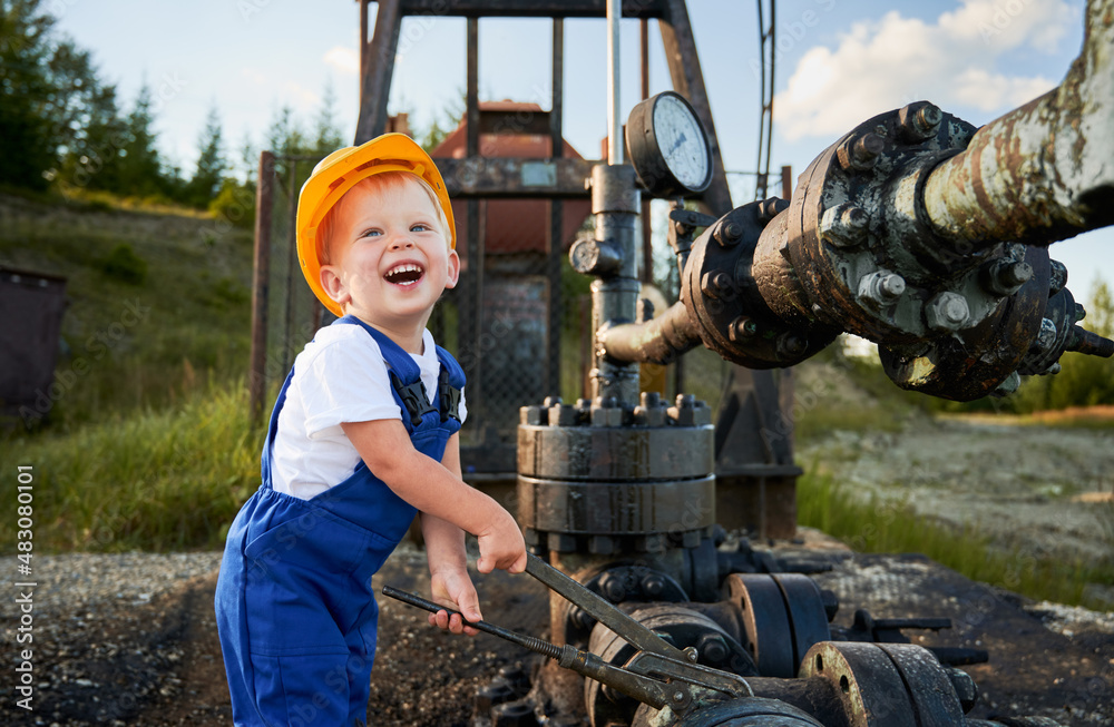 Happy male child playing in the mechanic, holding wrench near pipeline ...
