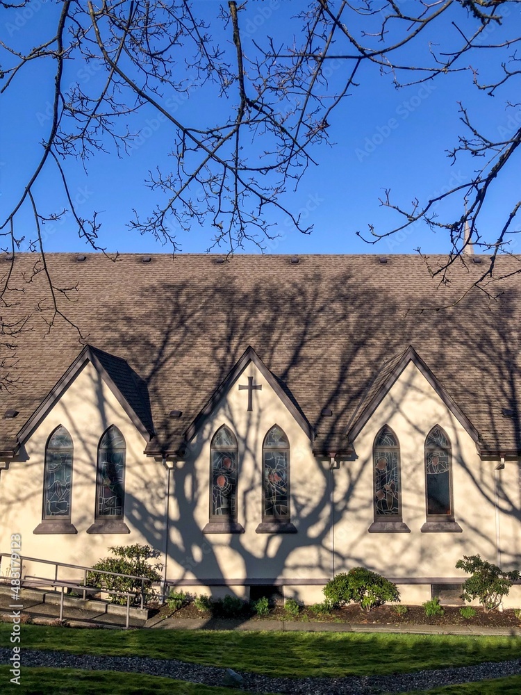 Tree shadows cast on a church wall with pitched roof and stained arch ...