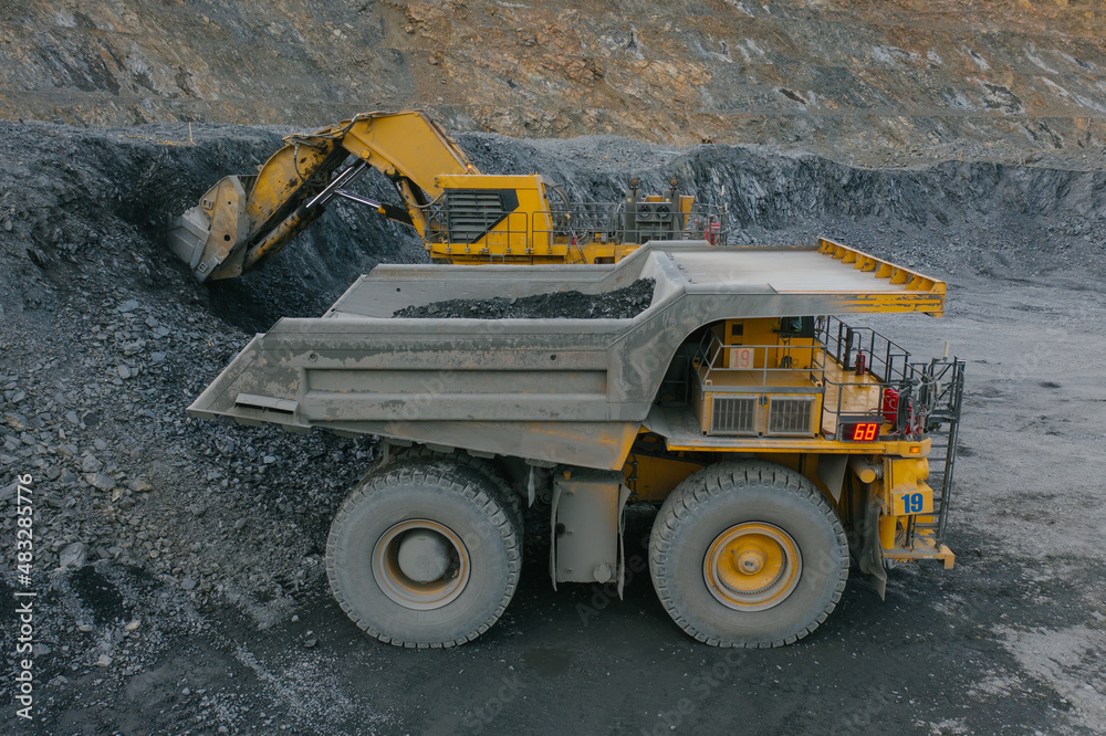 A heavy excavator loads ore into an open-pit dump truck at a gold mine ...
