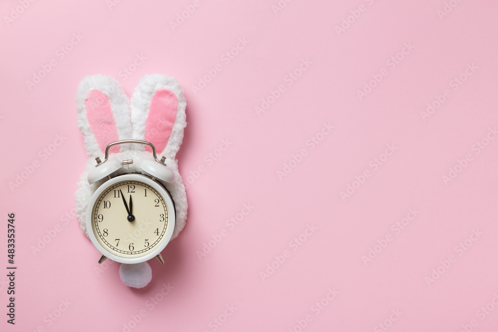 Alarm clock in easter bunny ears on a pink background with copy space ...