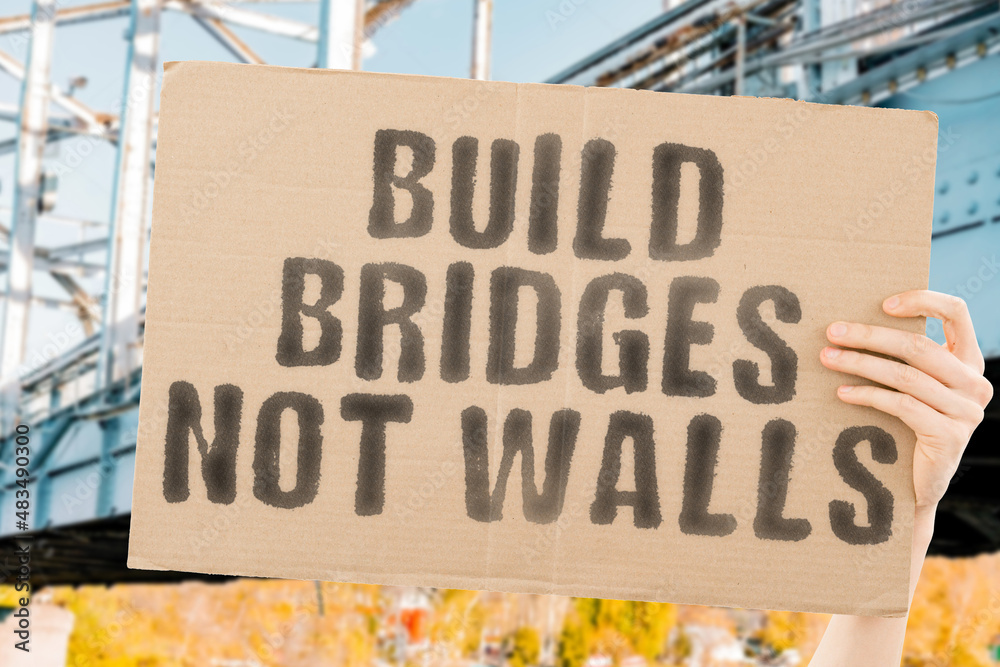The phrase " Build bridges not walls " on a banner in men's hand with ...