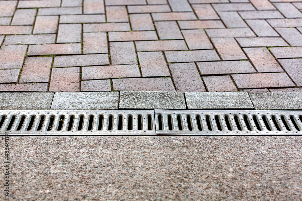 Pavement drainage grate with line iron grill on rectangular mosaic tile ...