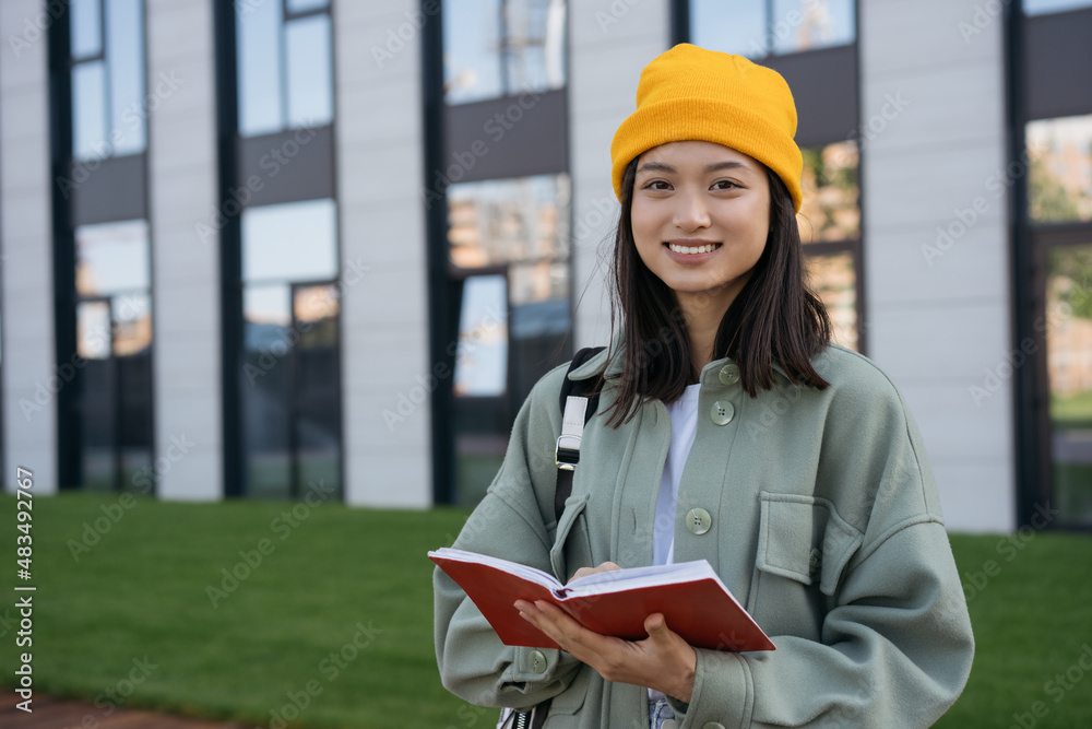 Smiling asian woman wearing stylish yellow hat holding holding book ...