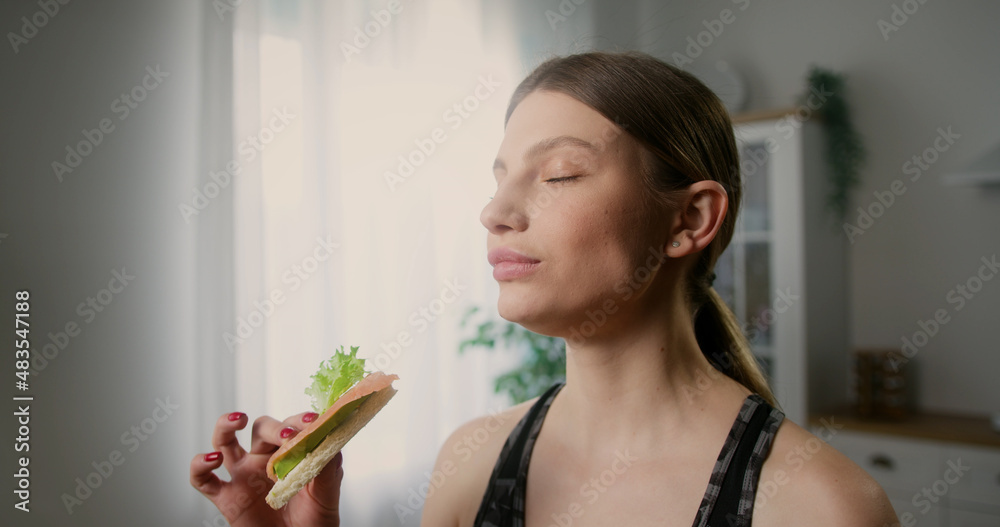 Zoom in shot of attractive young woman snacking on sandwich closing ...