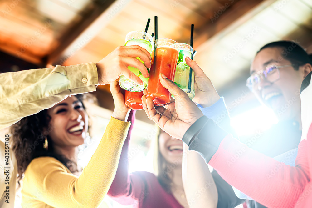 Happy friends cheering and drinking coloured cocktails in the pub ...