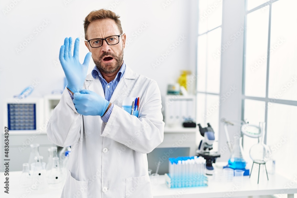 Middle age man working at scientist laboratory in shock face, looking ...