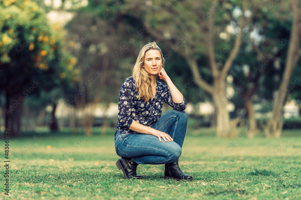blonde-haired woman poses for the camera squatting in a park Stock ...